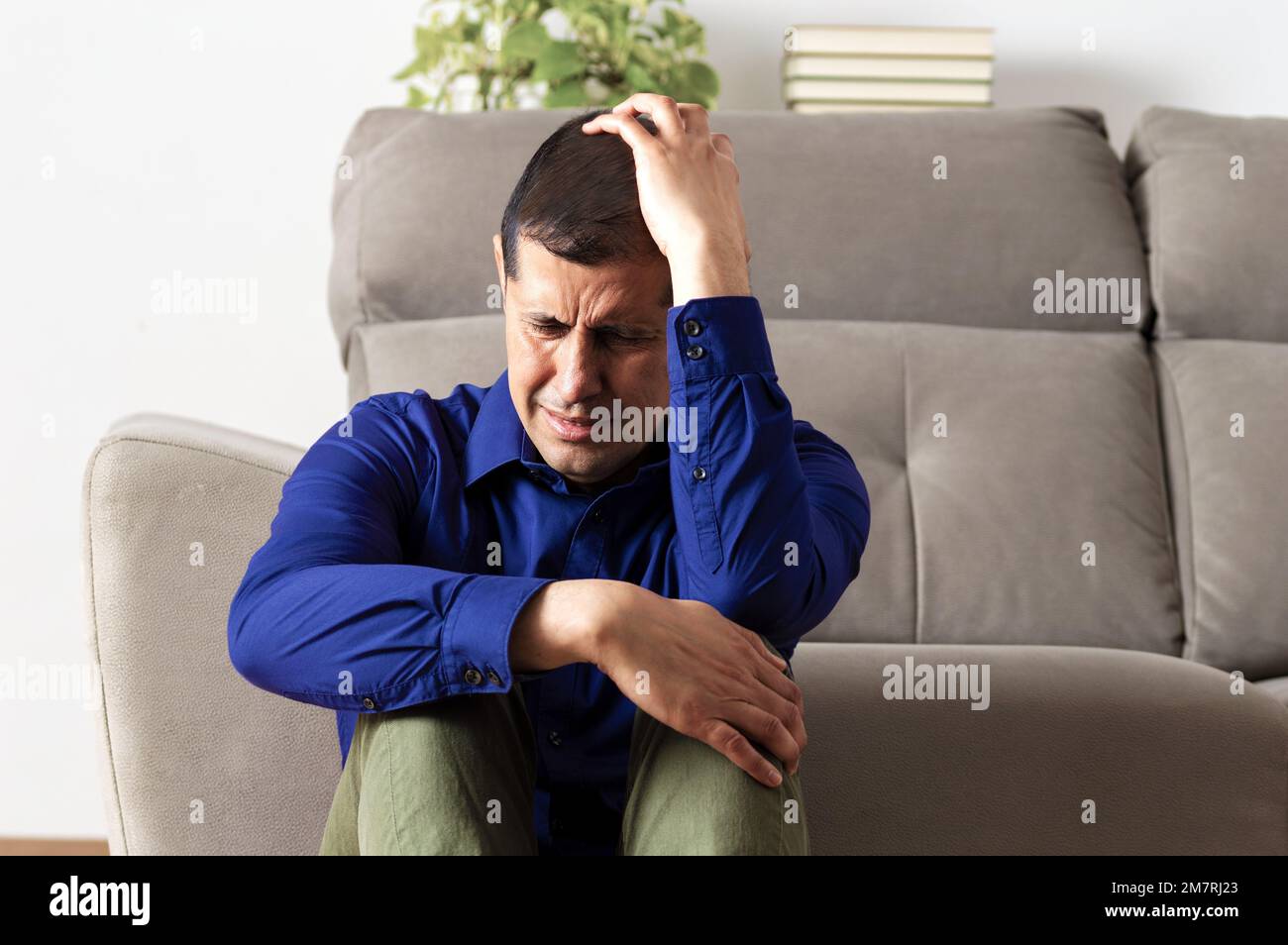 Sad man lamenting sitting on the floor in the living room in a house ...