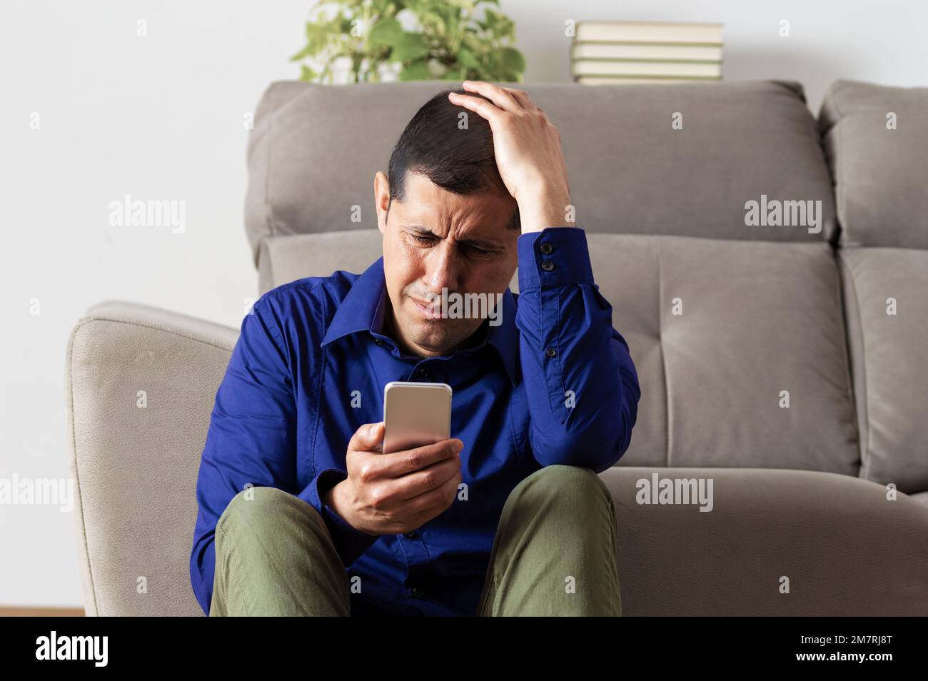 Single sad man checking mobile phone sitting on the floor in the living ...