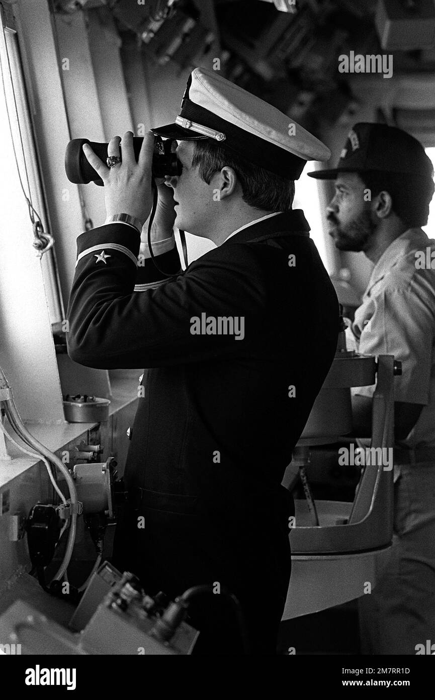 An ensign uses binoculars on the bridge of the destroyer USS JOHN ...