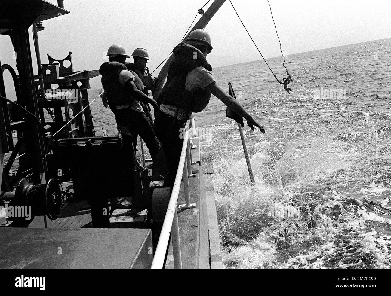 Three crewmen aboard minesweeping boat 51 (MSB-51) look toward the ...