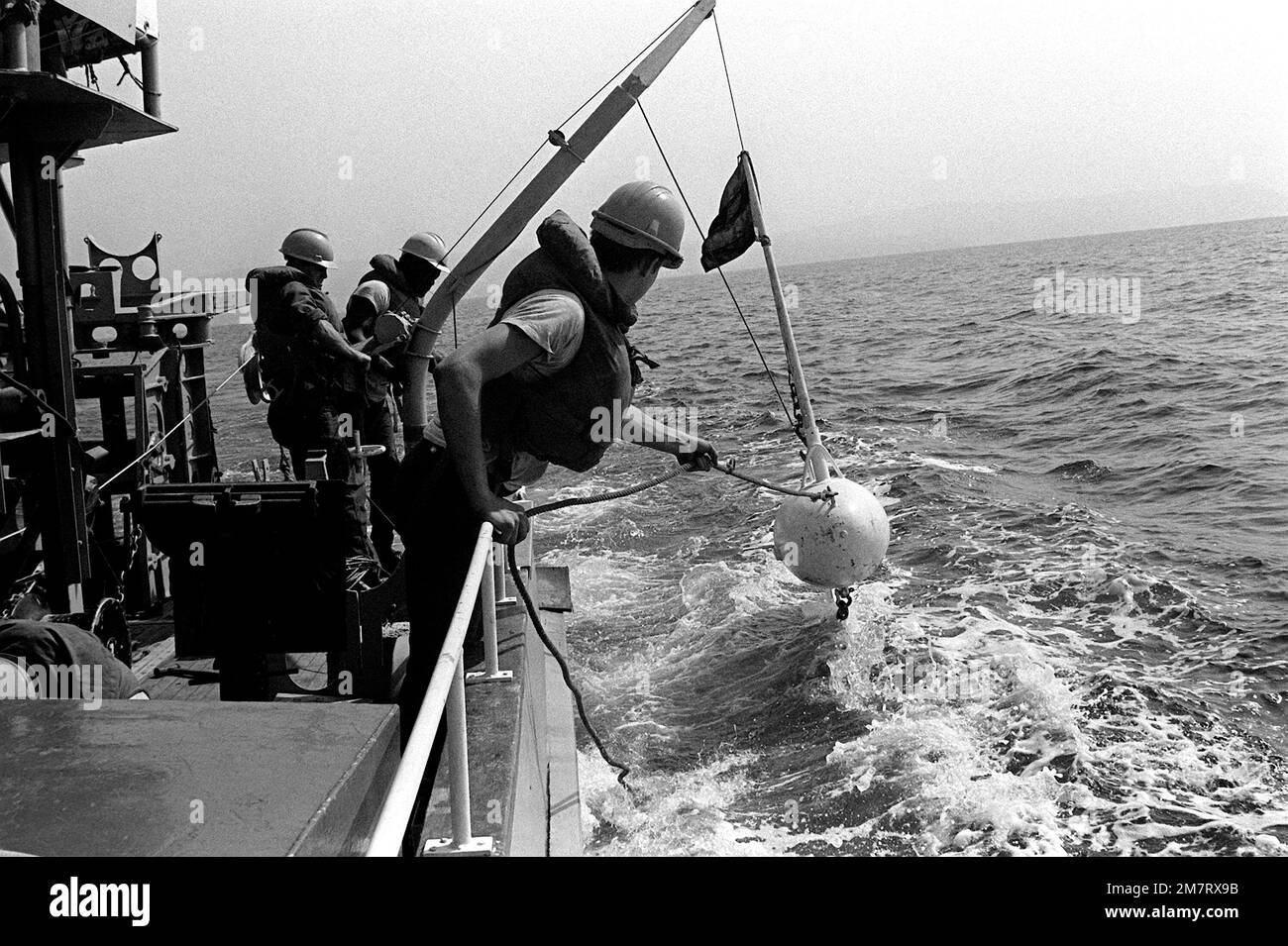Three crewmen aboard minesweeping boat 51 (MSB-51) prepare to drop a ...