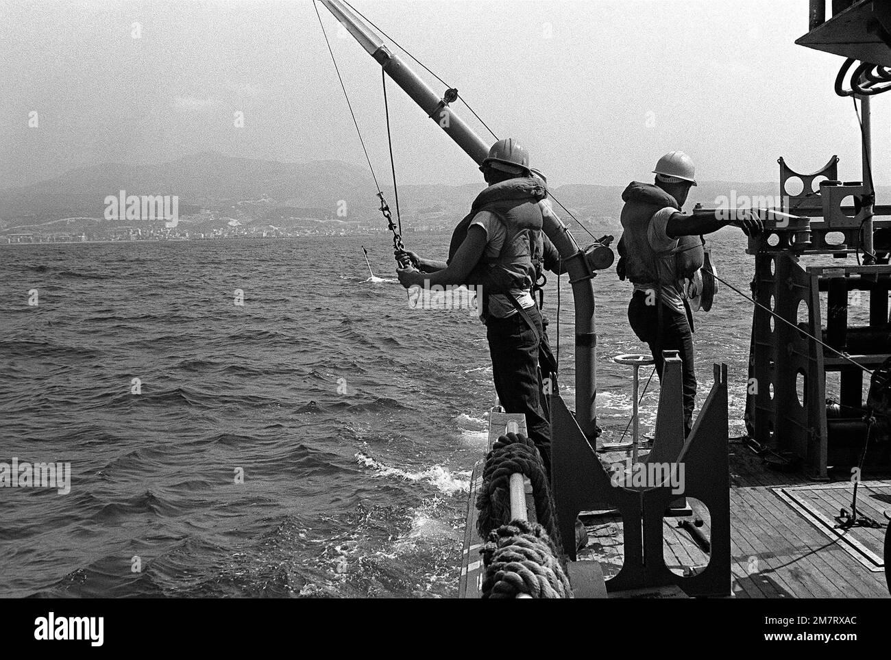 Two crewmen aboard minesweeping boat 51 (MSB-51) look toward the water ...