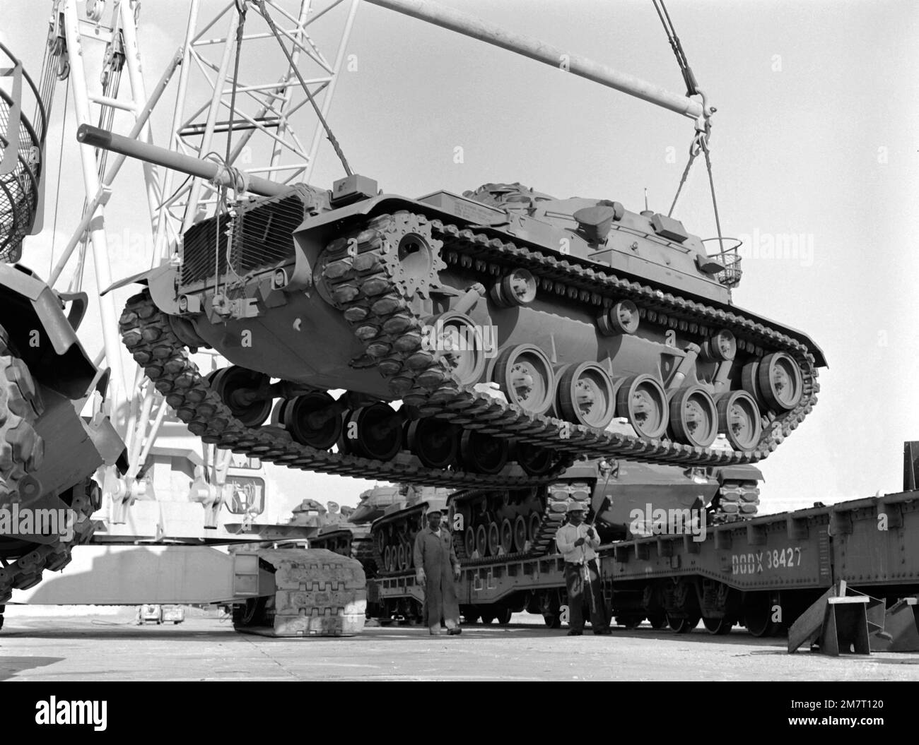 Base workmen use a huge crane to load M-60A1 tanks aboard railroad flat ...