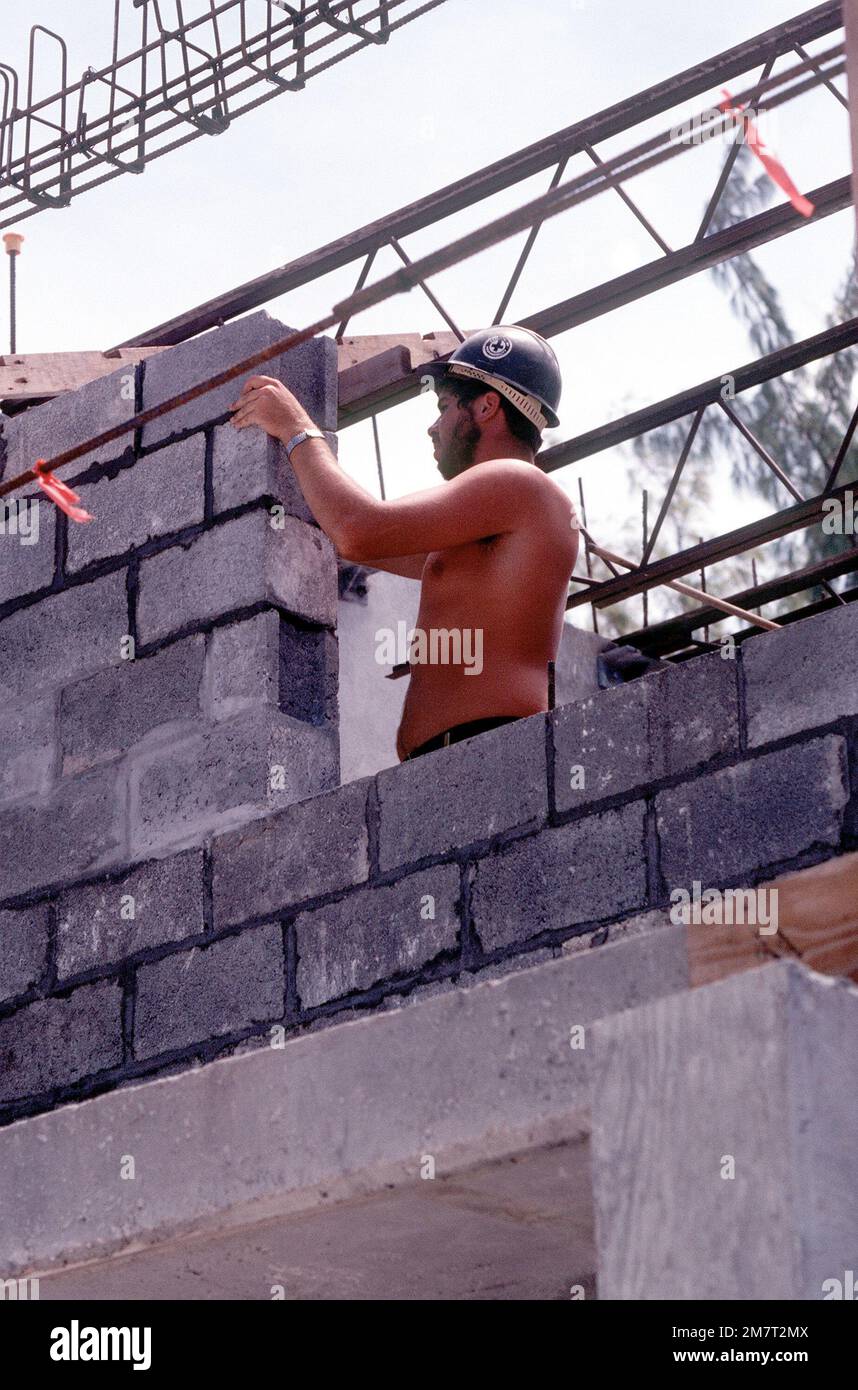 A Seabee positions a concrete block during construction of a building ...