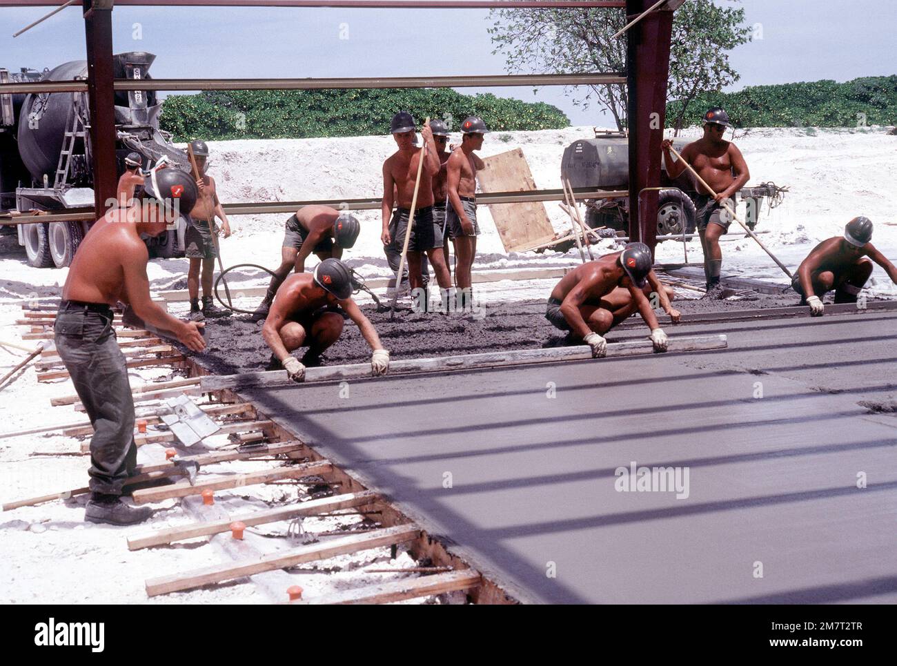 Seabees use a strike board to smooth concrete during construction of a ...