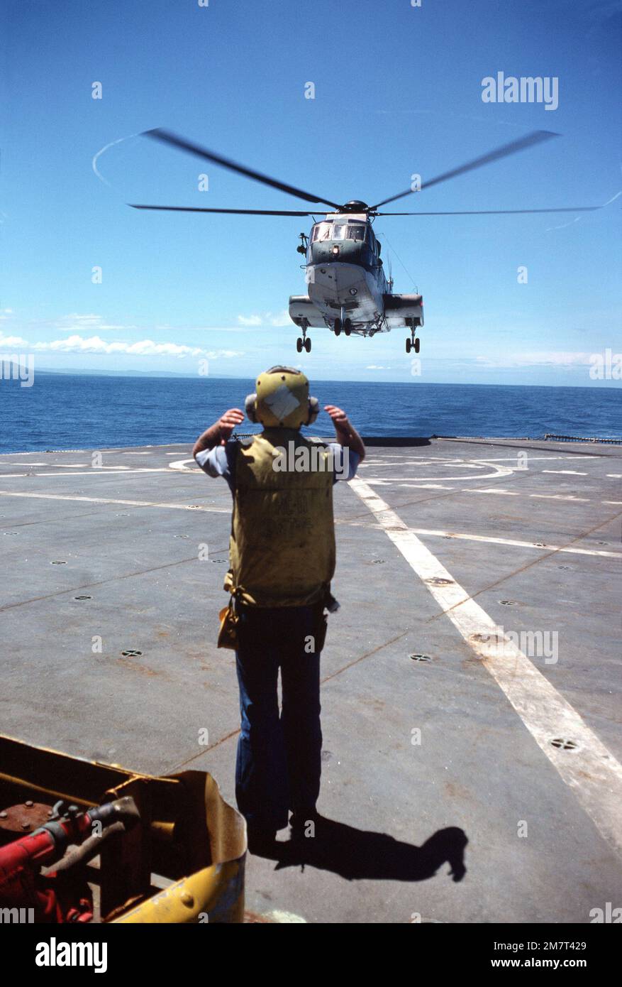 A flight deck crewmen directs an HH-3 Jolly Green Giant helicopter in for a landing aboard the ...