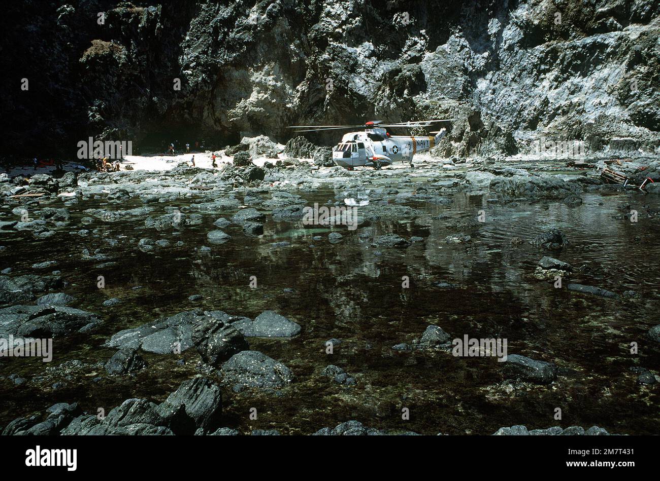 An SH-3 Sea King helicopter flies low over the shallow water looking ...