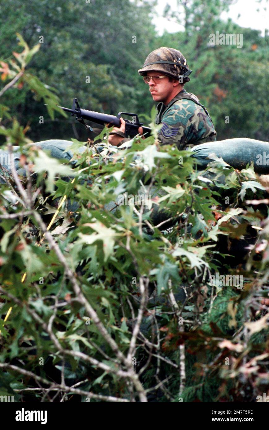 An airman armed with an M16 rifle guards, from a camouflaged position ...