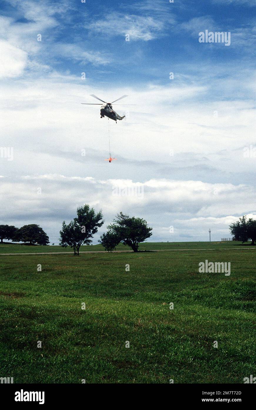 A ground-to-air view of an SH-3 Sea King helicopter airlifting a ...