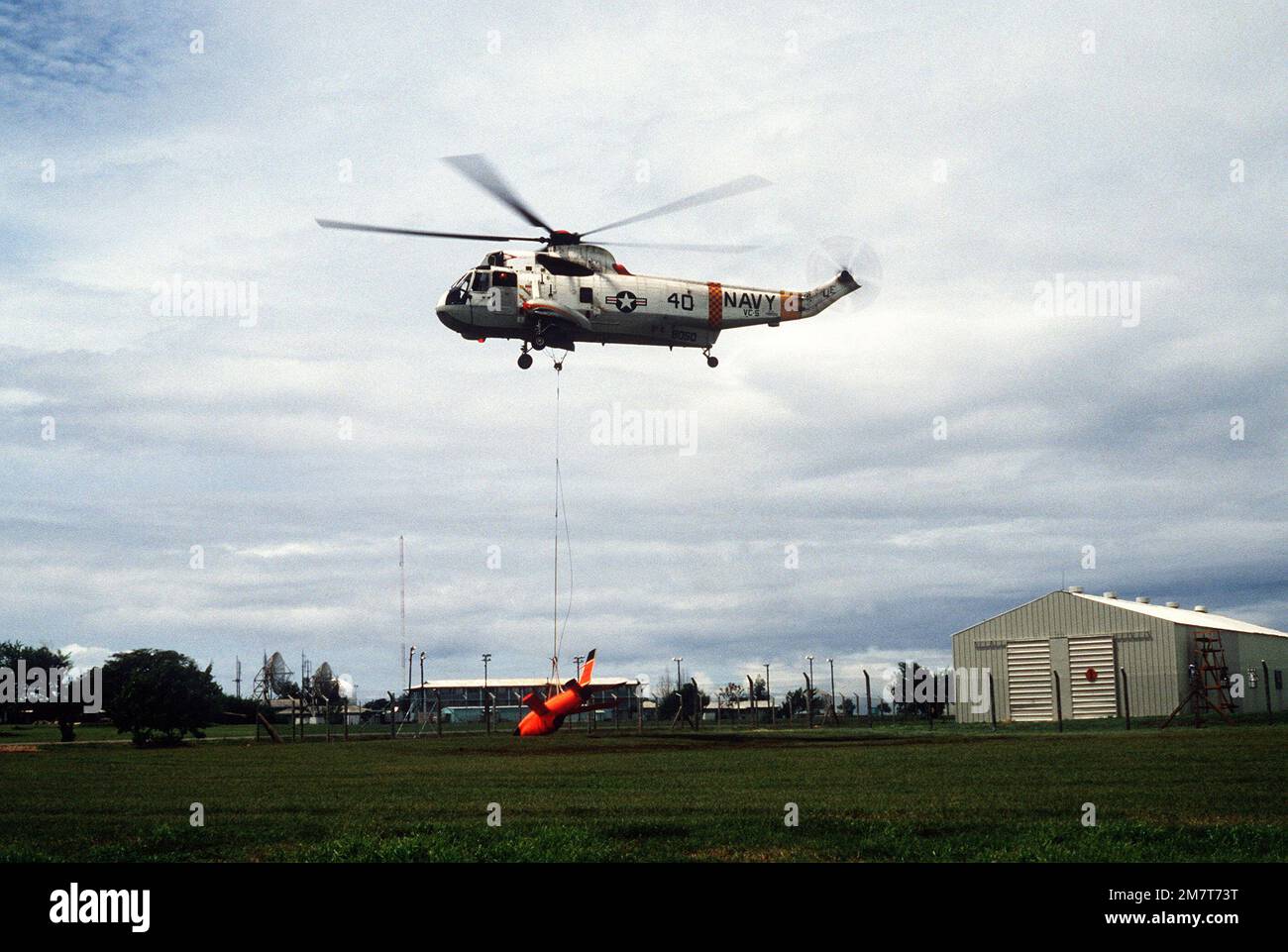 A ground-to-air left side view of an SH-3 King helicopter airlifting a ...