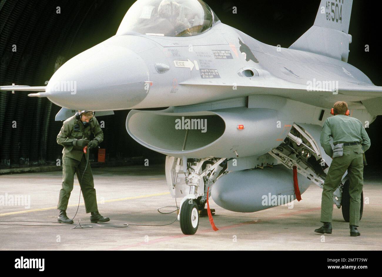 A ground crew chief and his assistant prepare to assist a pilot out of ...