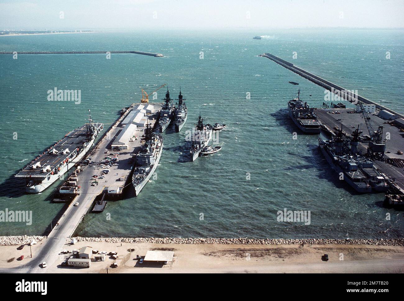 A view of ships docked at the pier as two tugboats nudge the destroyer ...