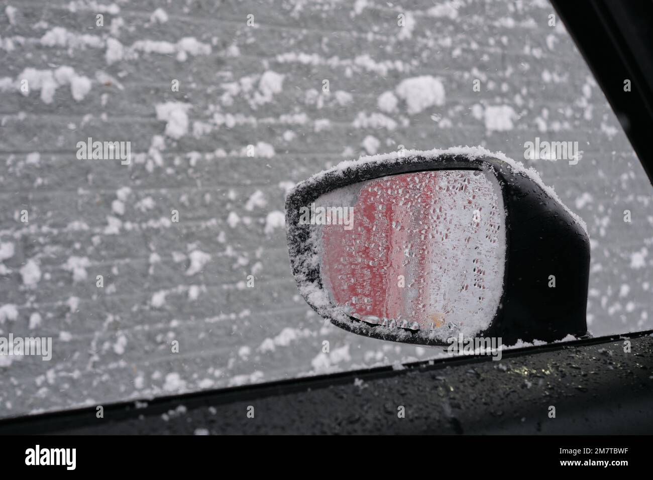 A side mirror is seen covered in wet snow through an open car window ...