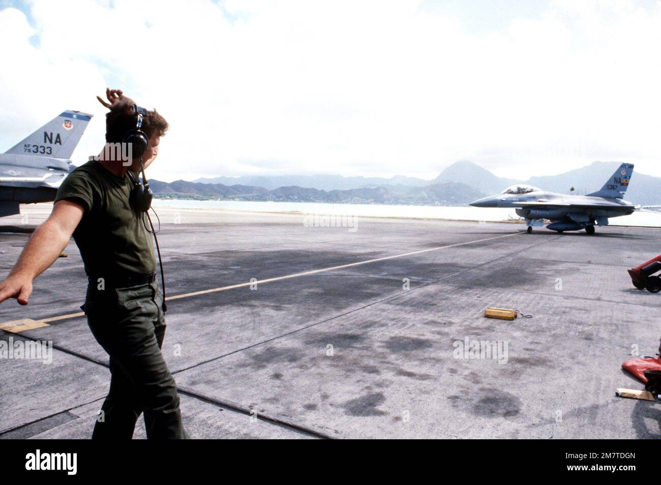 A ground crewman marshals an F-16 Fighting Falcon aircraft into a ...