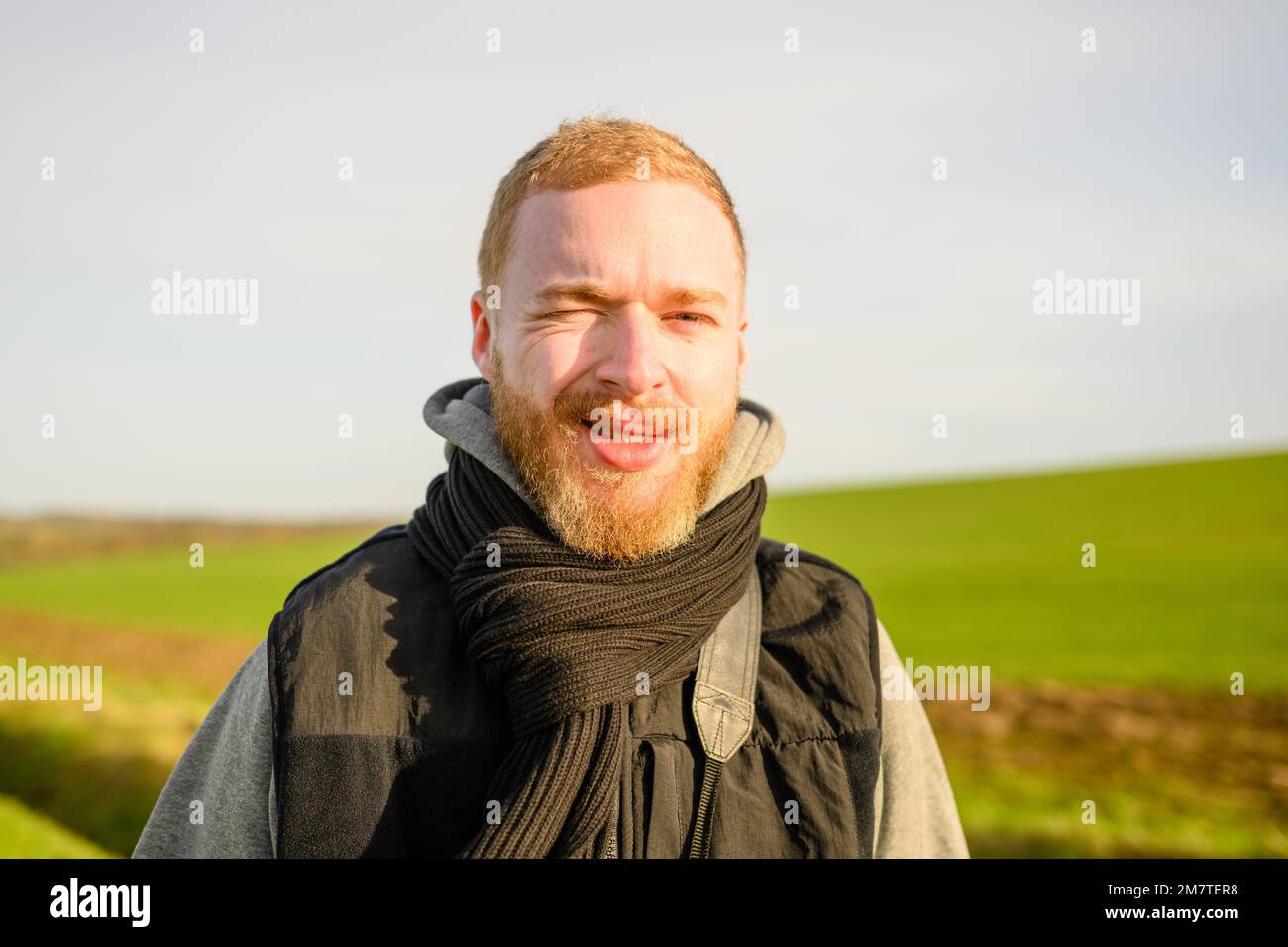 A caucasian man standing in a field staring at camera with one eye ...