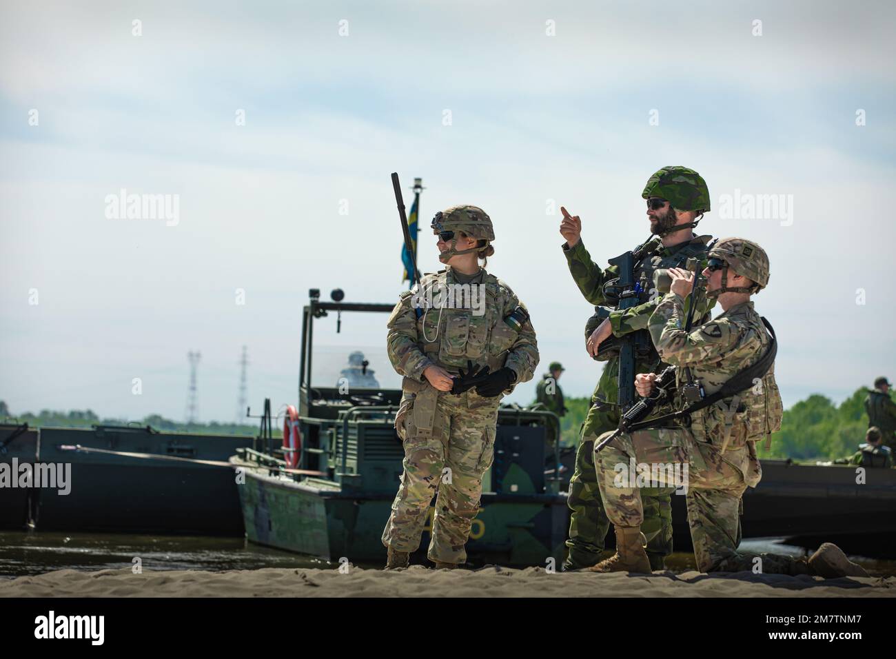 U.S. and Swedish soldiers look at passing boats during a wet-gap ...