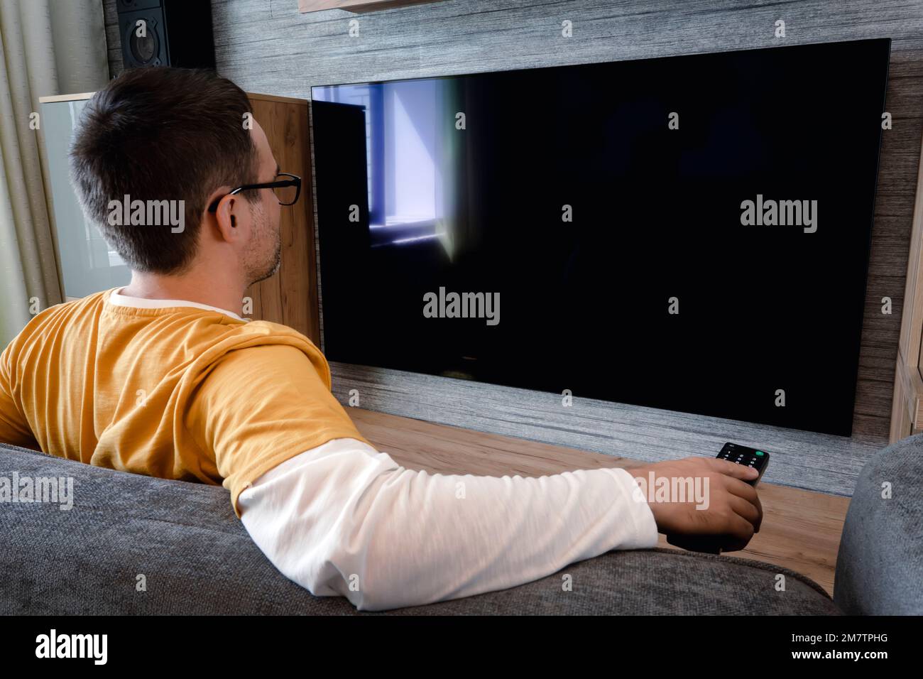 Man watching television, turning on plasma flatscreen TV-set, pointing remote control at empty ...