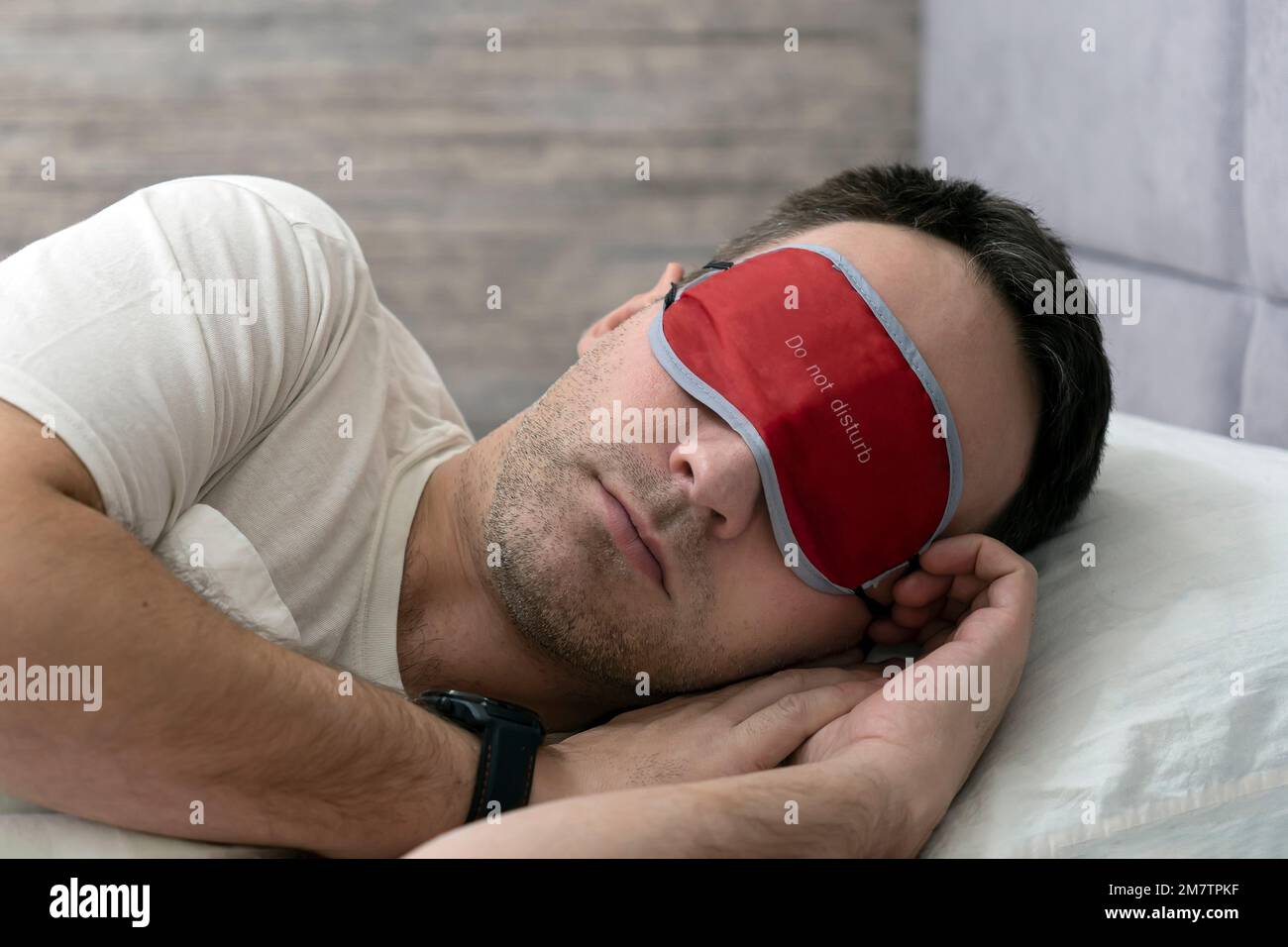 Calm caucasian young man in sleep mask white t-shirt lying in bed ...