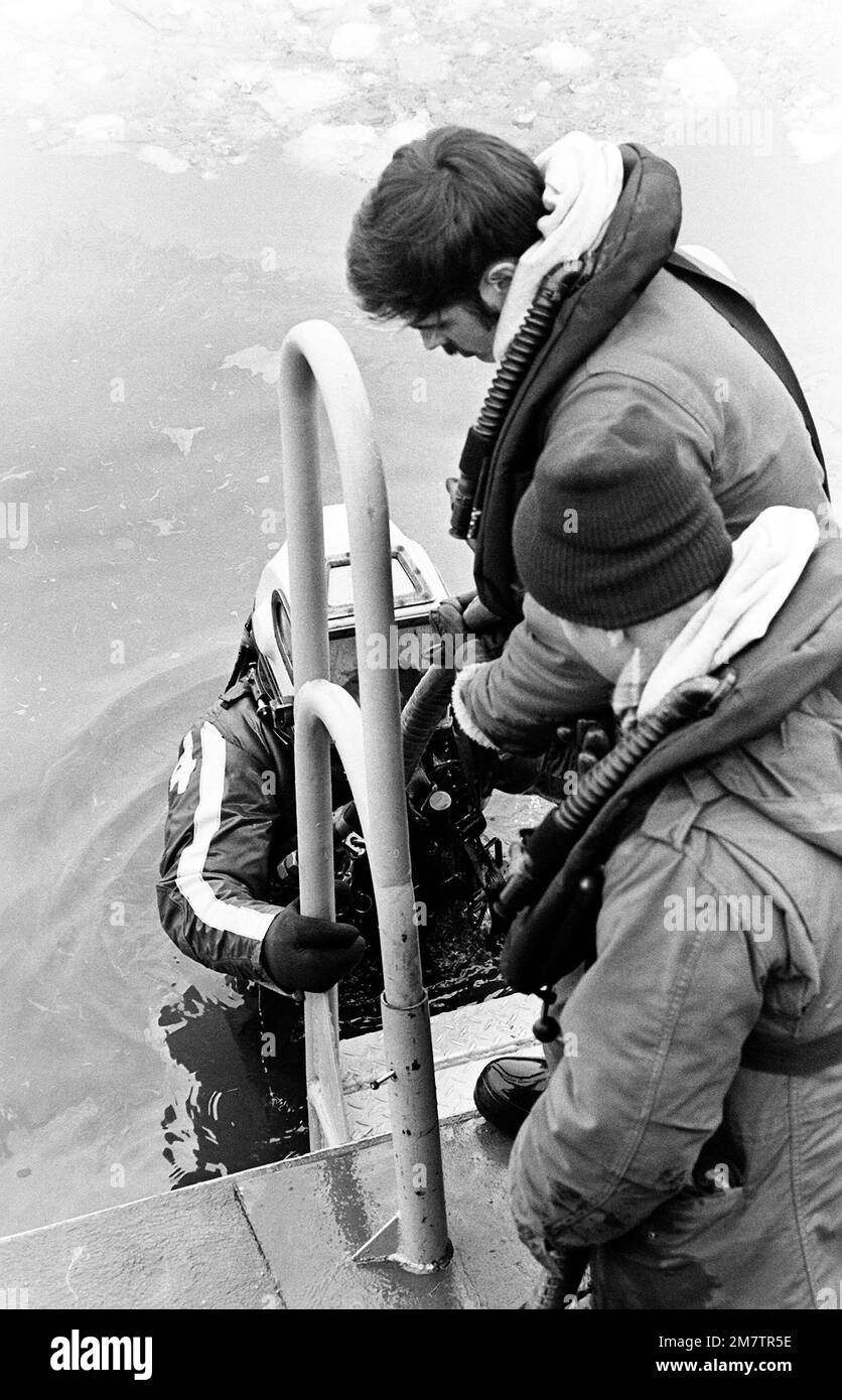 Two Navy divers assist another out of the water at the completion of ...
