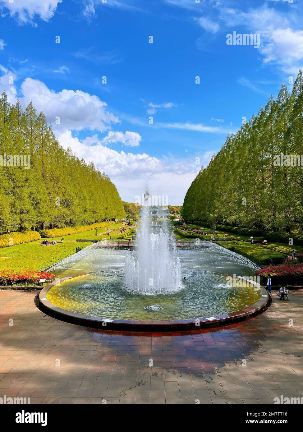 A vertical shot of a fountain in Sagamihara Park with a cloudy blue sky ...