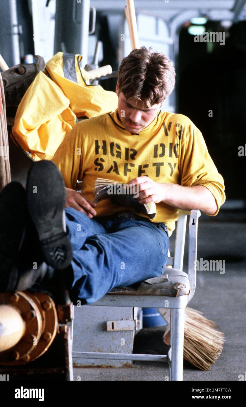 A crewman takes a break by reading a book aboard the aircraft carrier ...