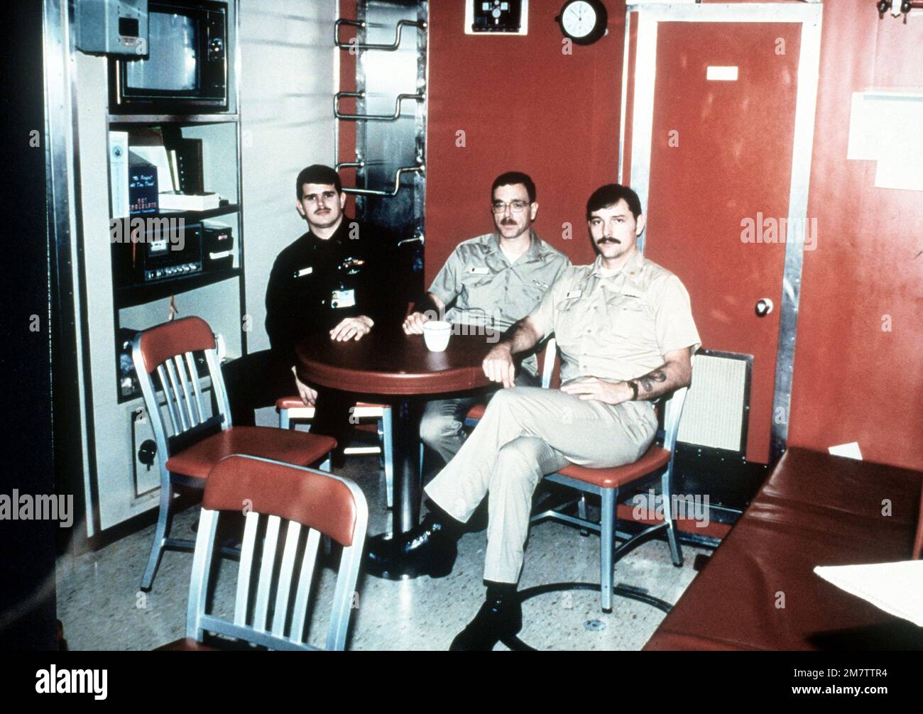 Three crewmen sit at a table in a chief petty officer's state room ...