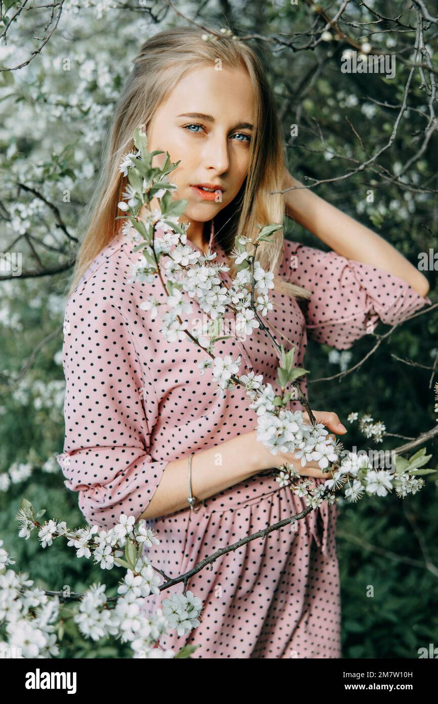 Blonde girl on a spring walk in the garden with cherry blossoms. Female ...