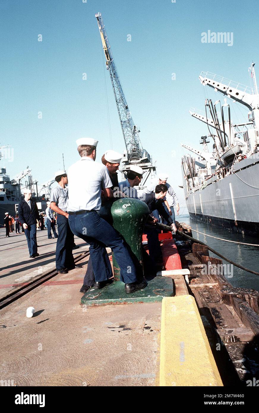 Sailors on the pier pull the lines during docking procedures for ...