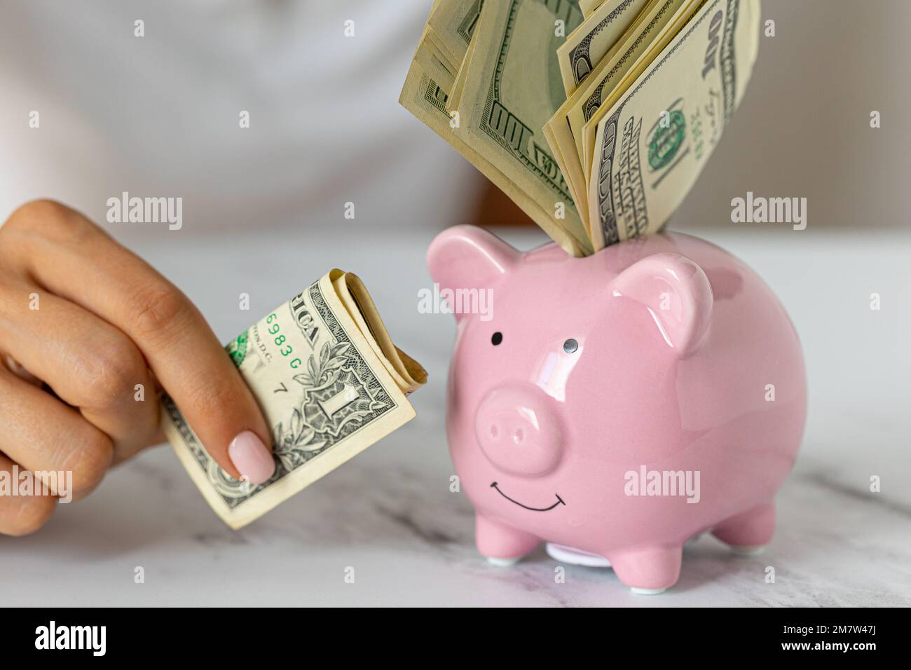 Close-up of a woman's hands put dollar paper money in a piggy bank ...