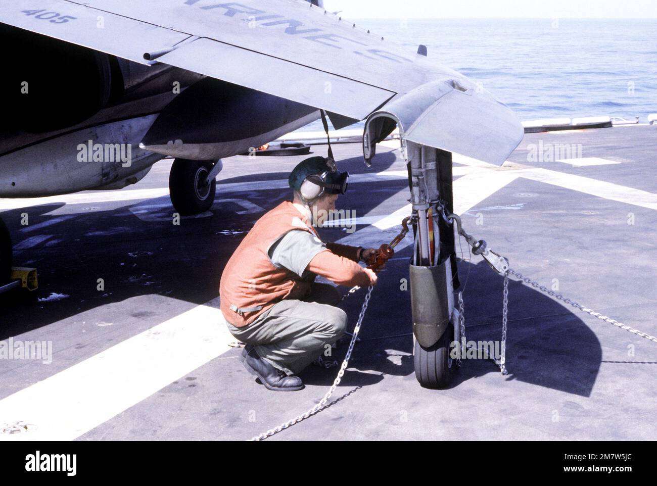 Tie-down chains are loosened on an AV-8A Harrier aircraft as ...