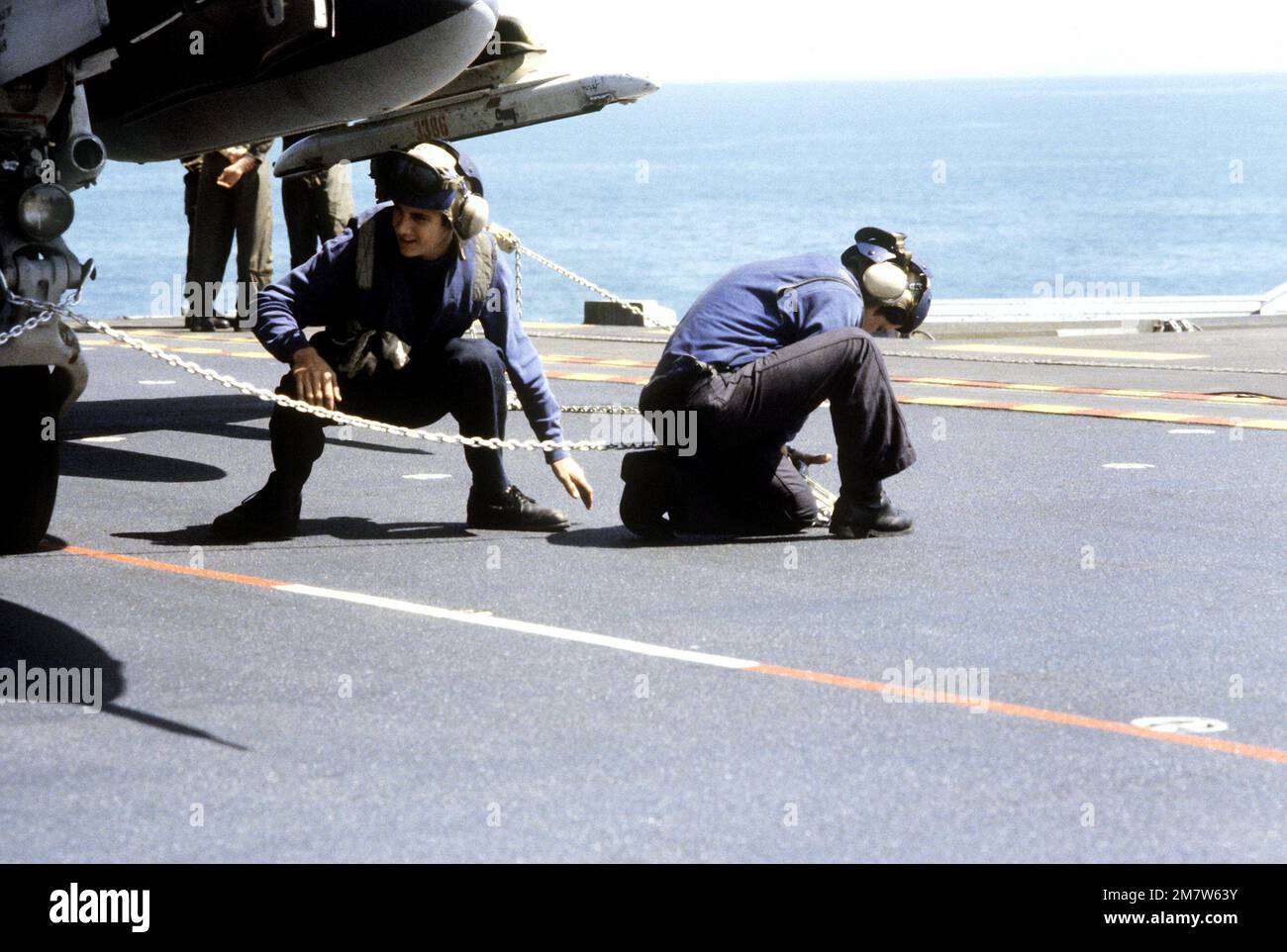 Flight deck crewmen loosen the tie-down chains as they prepare an ...
