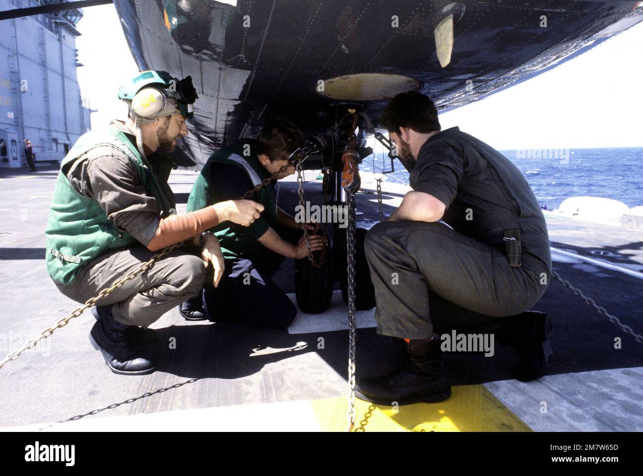 Flight deck crewmen check the tires of a parked aircraft on the deck of ...