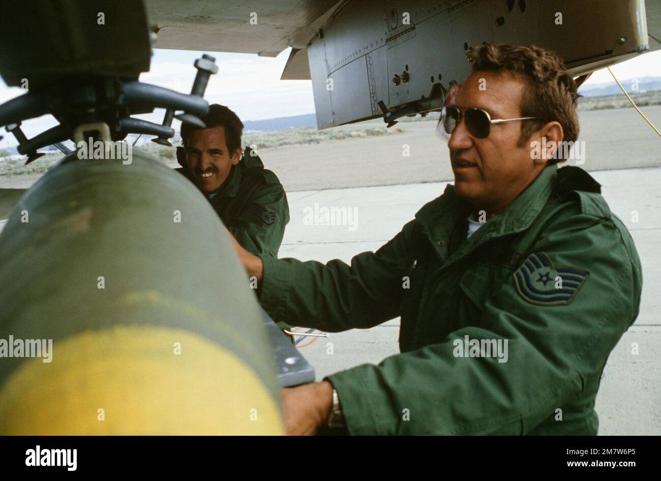 Weapons technicians upload a bomb onto the wing pylon of an A-7D ...