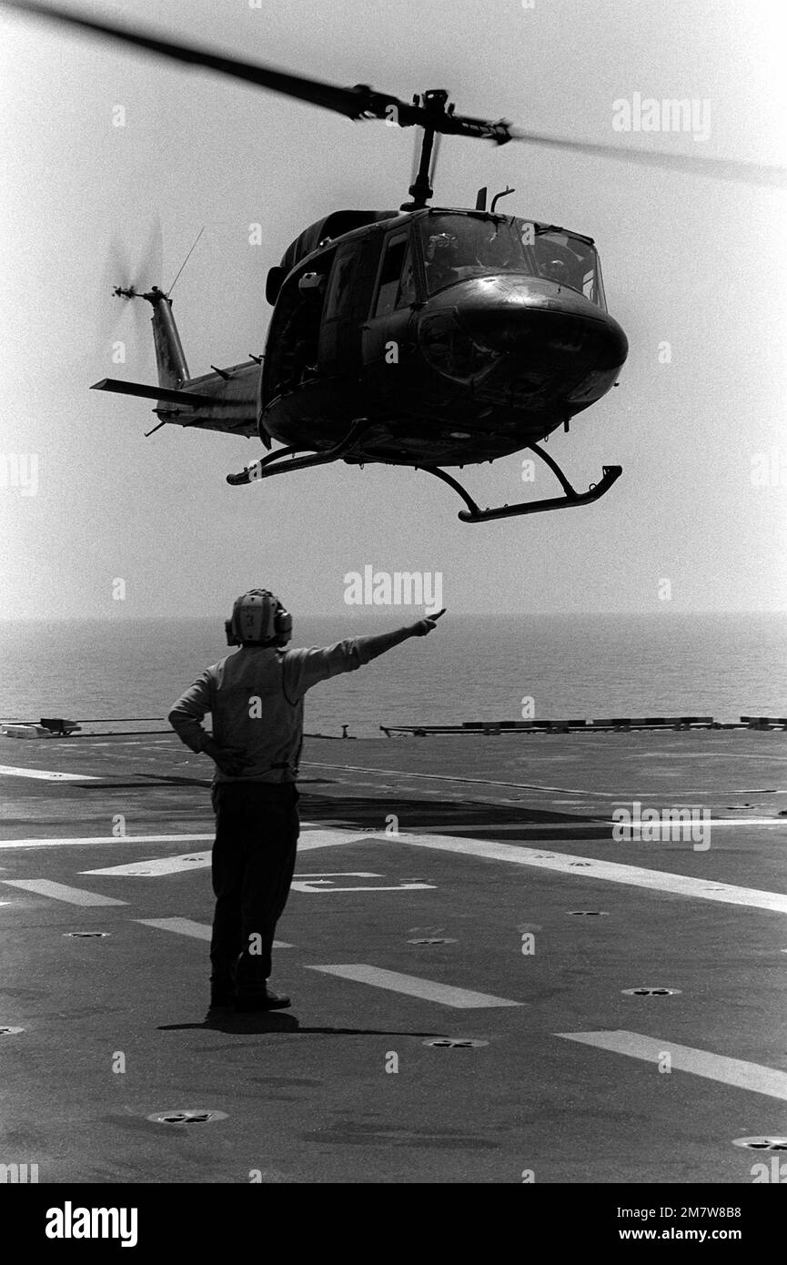 A flight deck crewman gives signals as a UH-1N Iroquois helicopter from ...