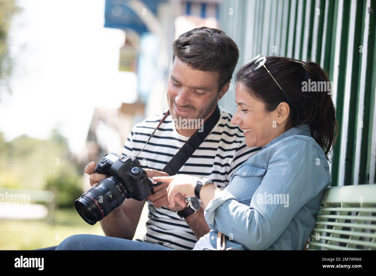 couple of tourists reviewing photos on camera sitting on bench Stock ...