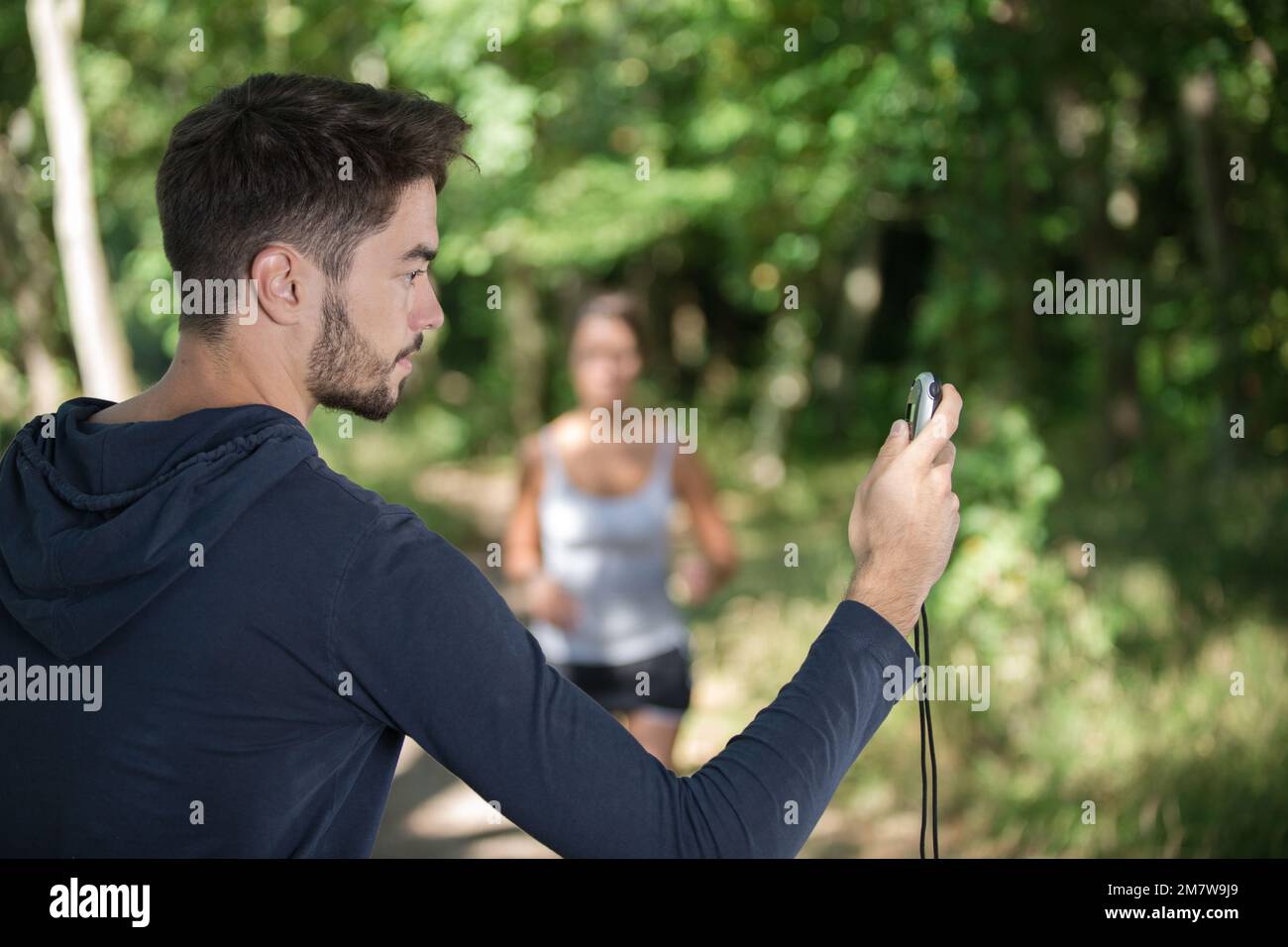 young coach measuring time for young woman running Stock Photo - Alamy