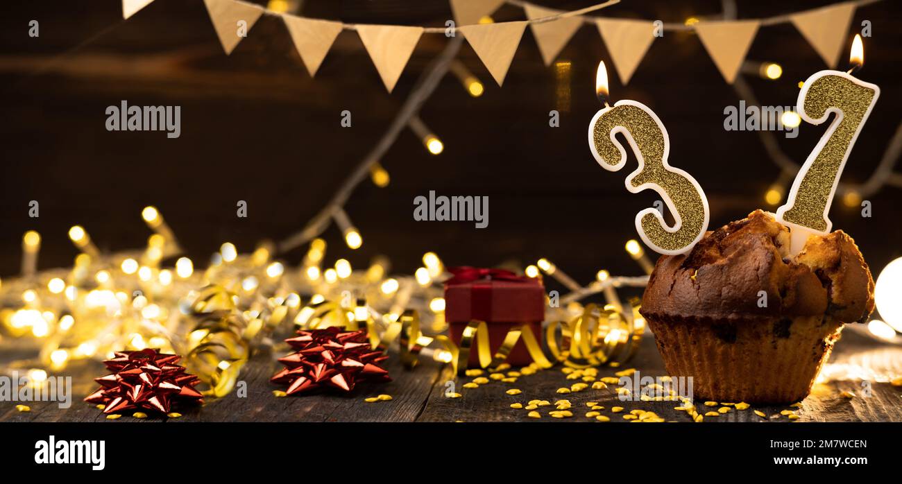 Number 37 birthday celebration candle in cupcake against lights and ...