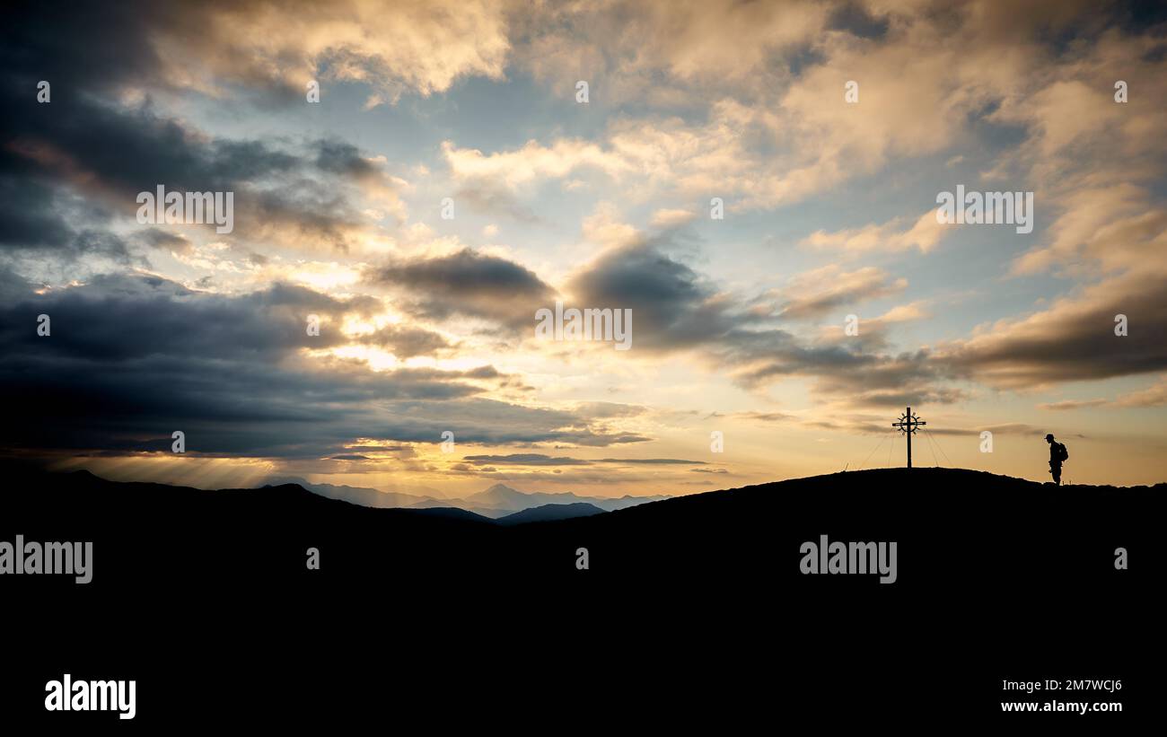 A beautiful shot of a silhouette of a hiker reaching a cross on a field ...