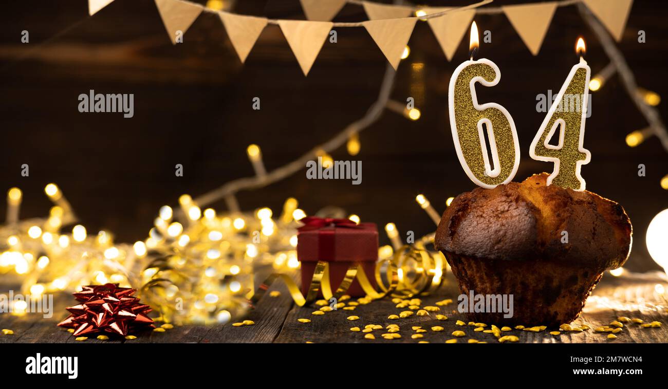 Number 64 golden festive burning candles in a cake, wooden holiday ...