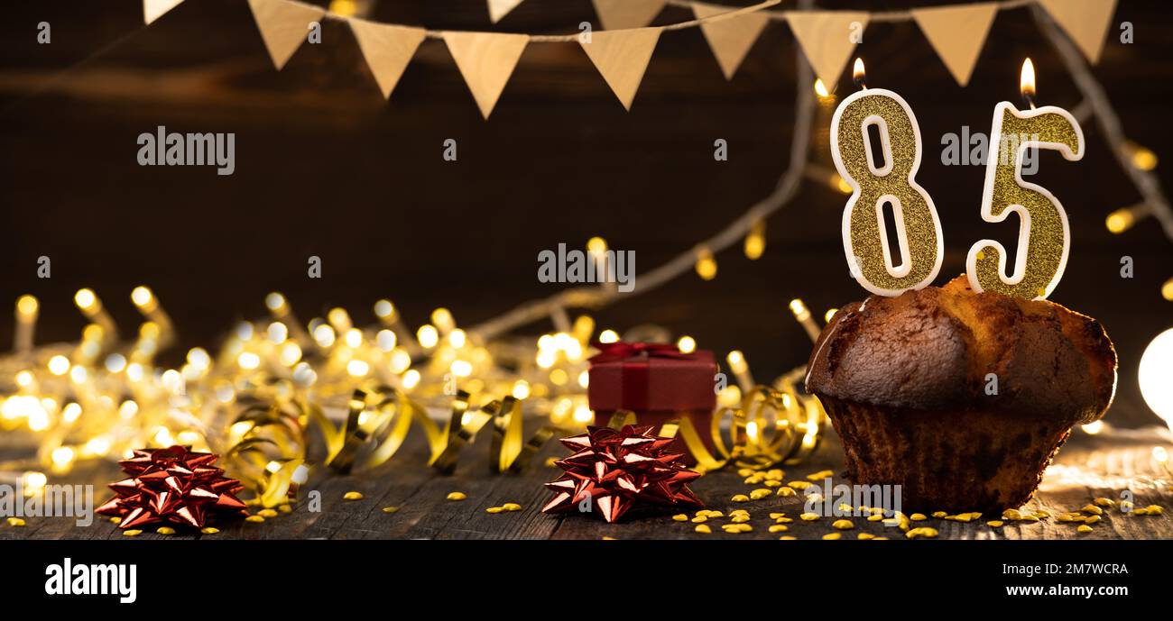 Number 85 golden festive burning candles in a cake, wooden holiday ...