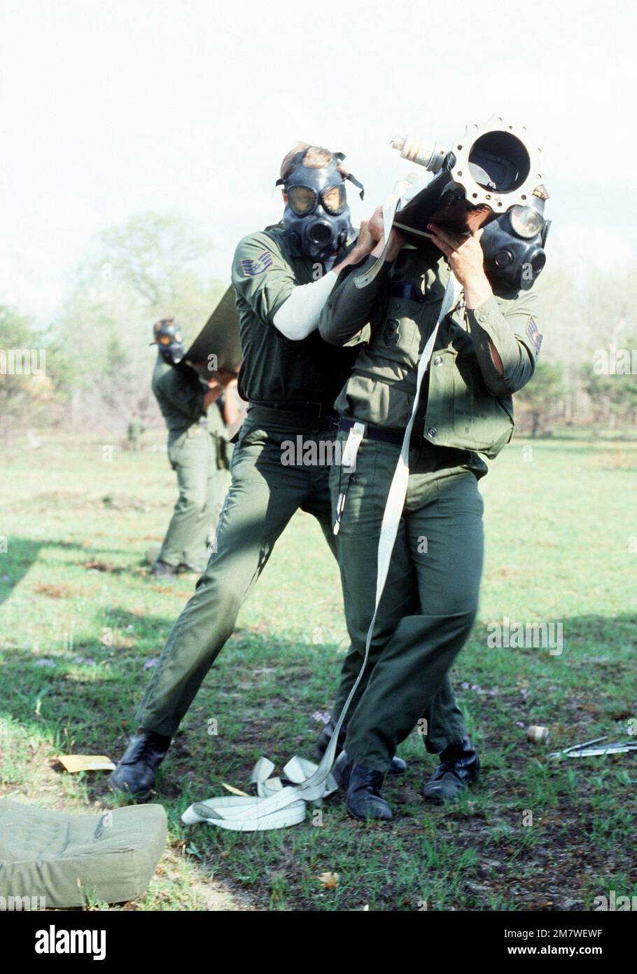 Crew members wearing gas masks, carry a rotor blade for an HH-3E Jolly ...