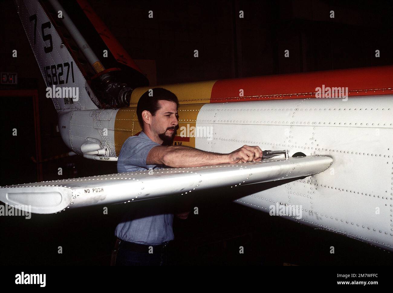 A Navy aircraft mechanic works on the tail section of a UH-1N Iroquois ...