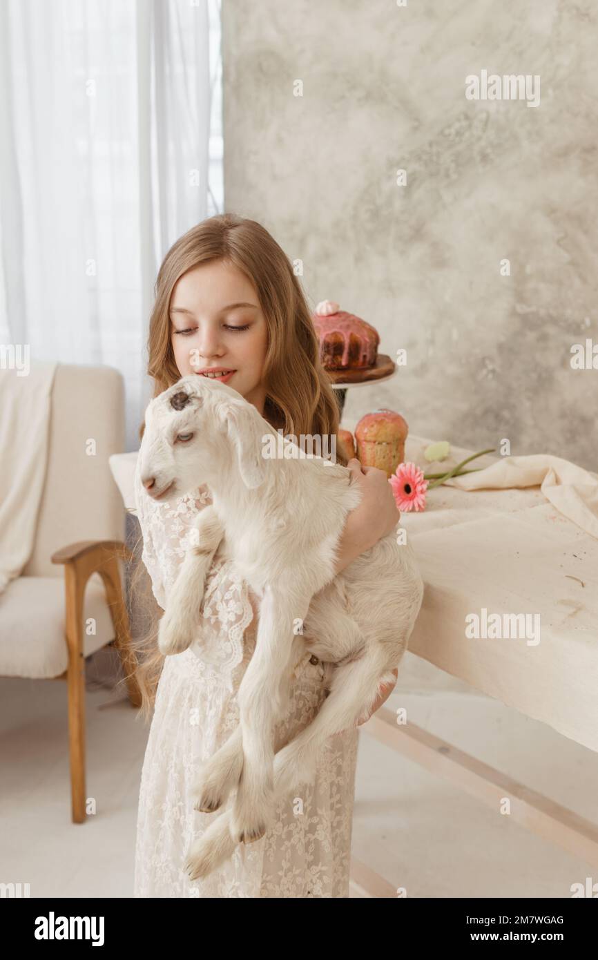 The girl is sitting at the Easter table with cakes, spring flowers and ...