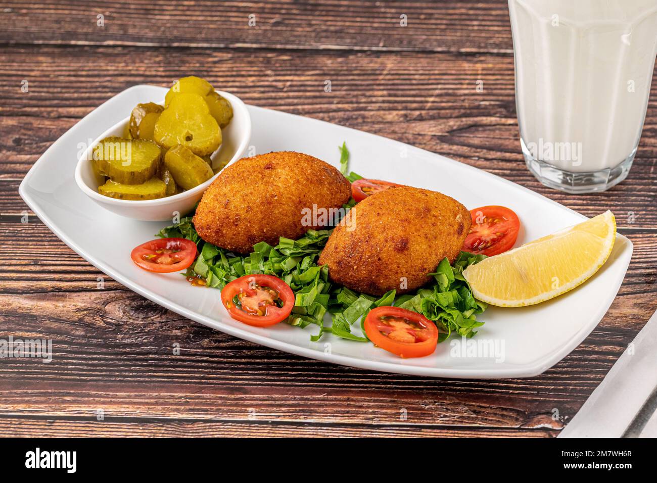 Kibbeh or icli kofte on a white porcelain plate with pickles and salad ...