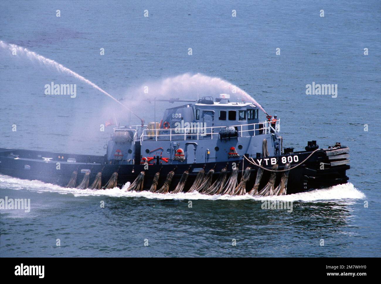 Crewmen aboard the large harbor tug (YTB 800) spray water into the air ...