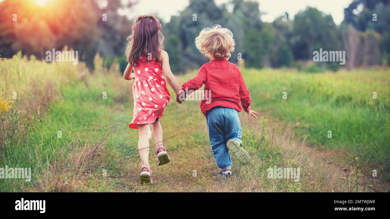 Little boy and girl holding hands run in the field on a sunny day back ...