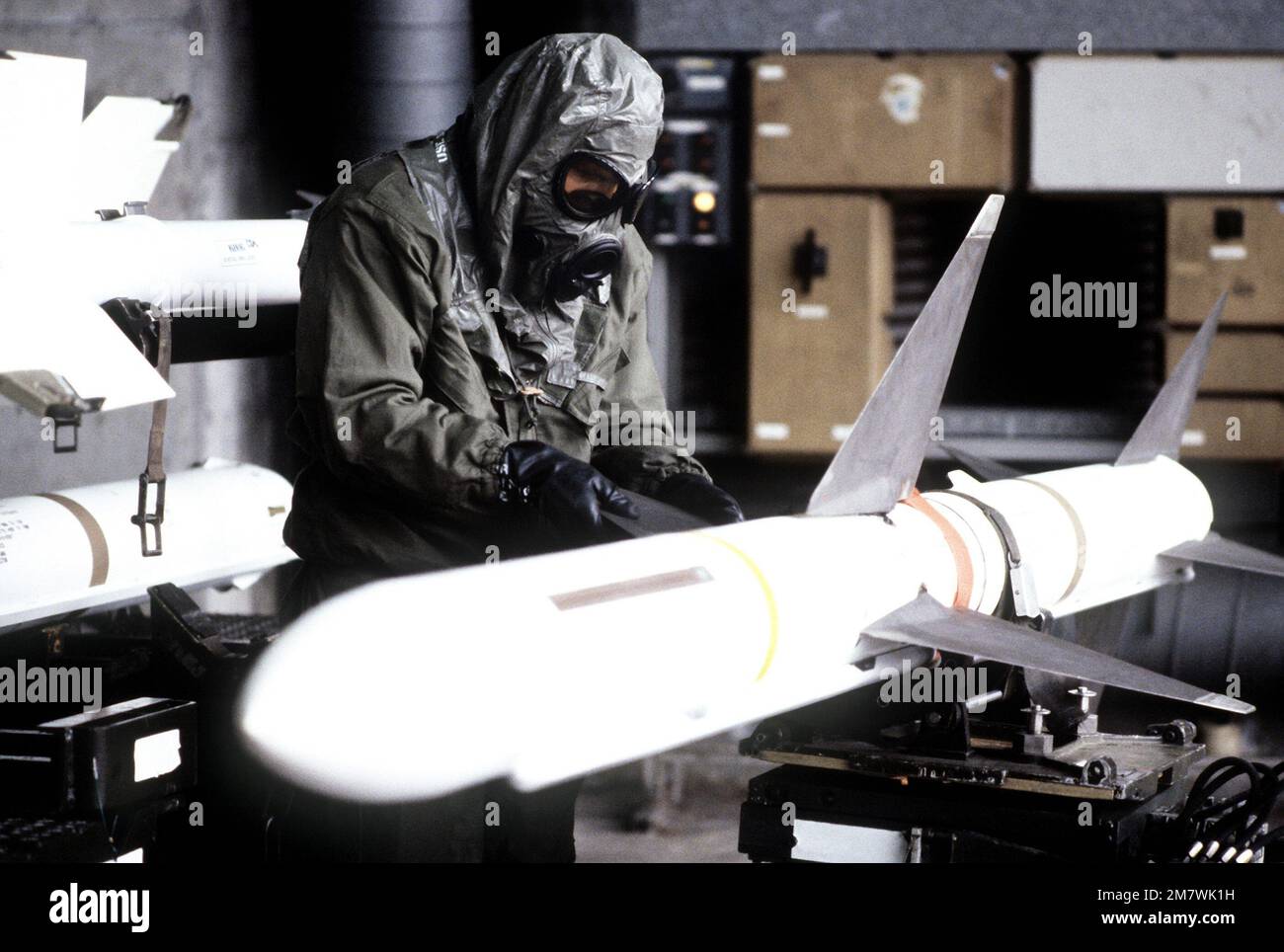 A technician in chemical warfare gear works on AIM-9 missiles during ...