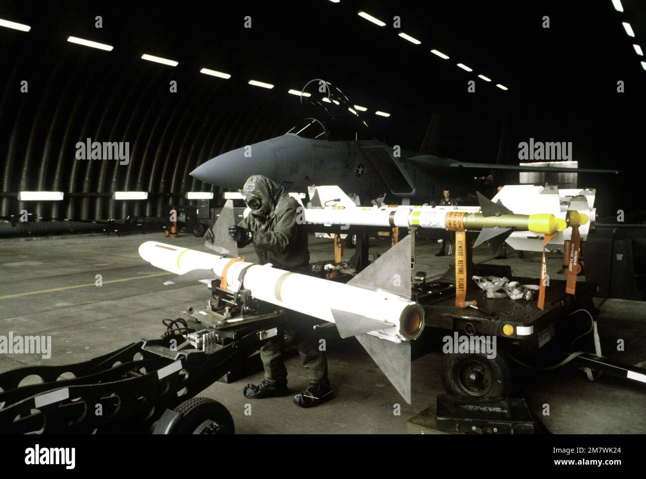 A technician in chemical warfare gear works on AIM-9 missiles during ...