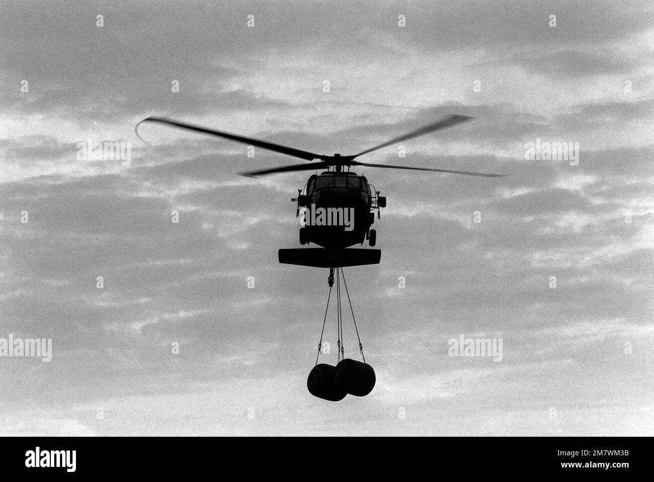 A UH-60A Black Hawk helicopter carries a sling load of fuel to be used ...