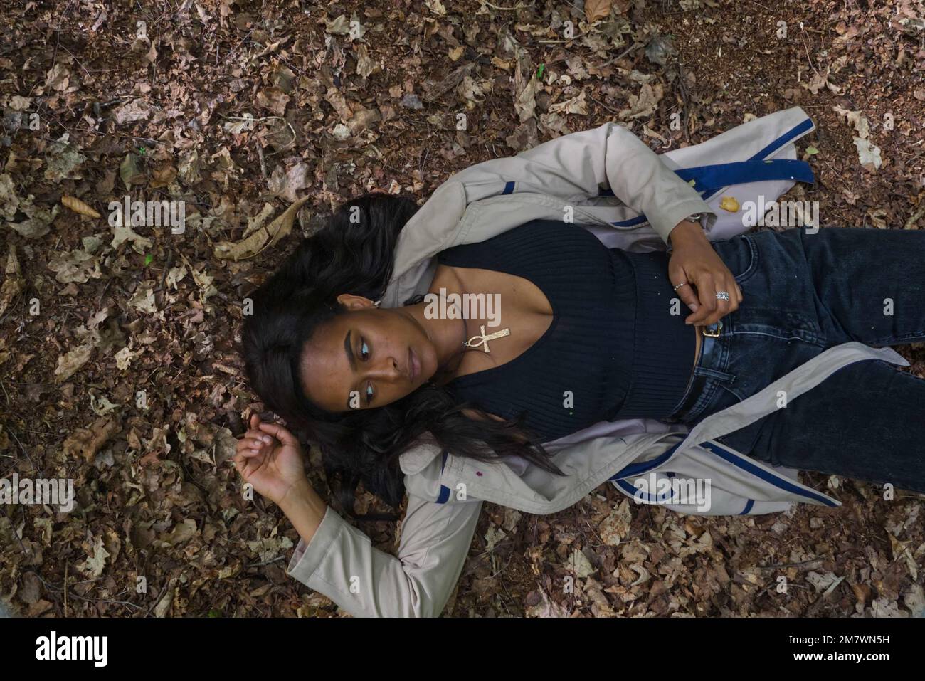 A young woman laying in the woods amongst the dead leaves. dressed in ...